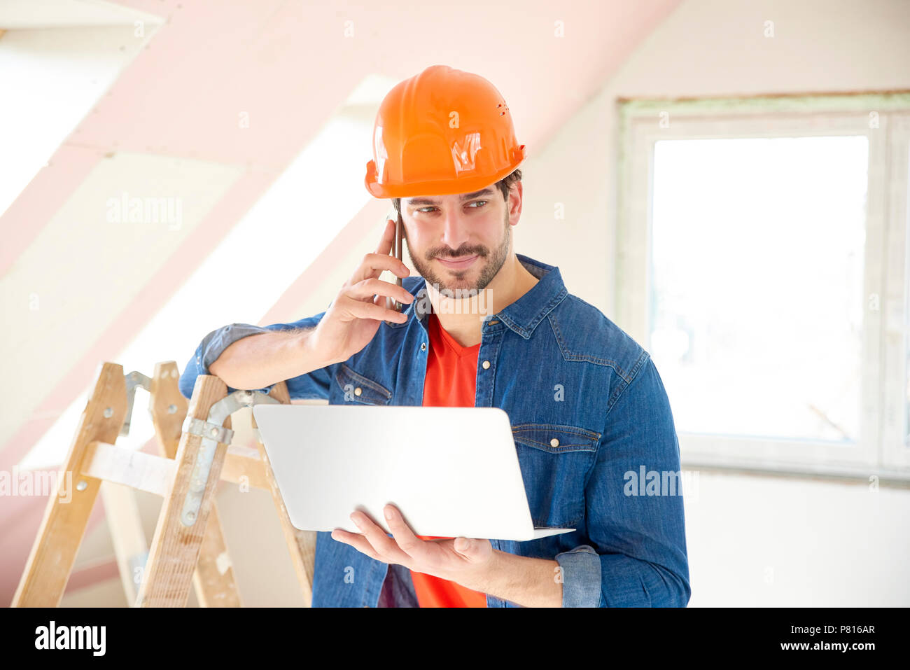 Young repairman using laptop and mobile phone while standing at ...