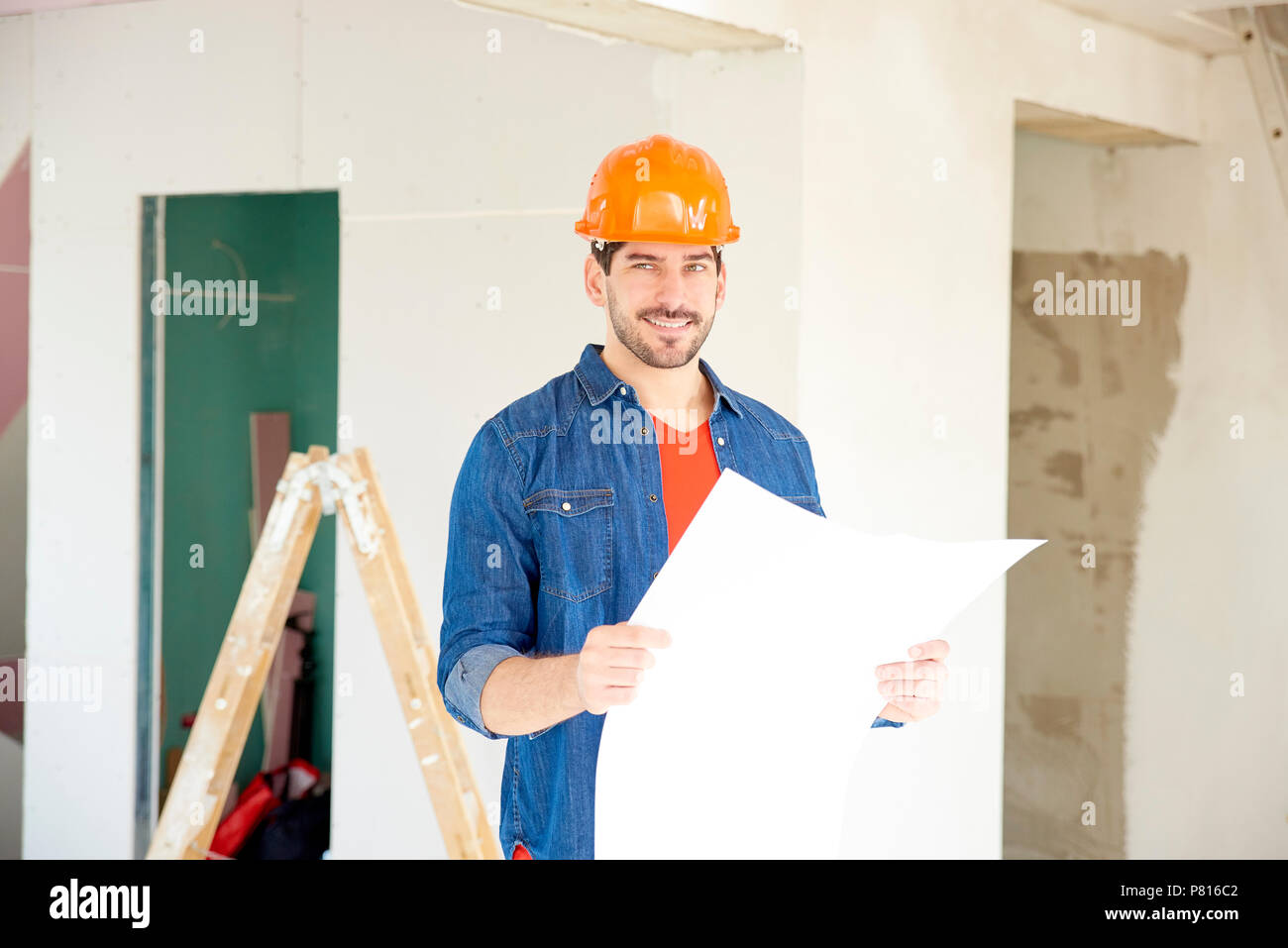 Portrait of happy engineer holding blueprint in his hand while standing ...