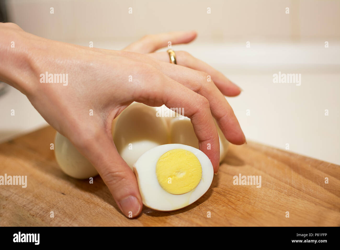 Hard-boiled egg cut in half held between the fingers Stock Photo - Alamy