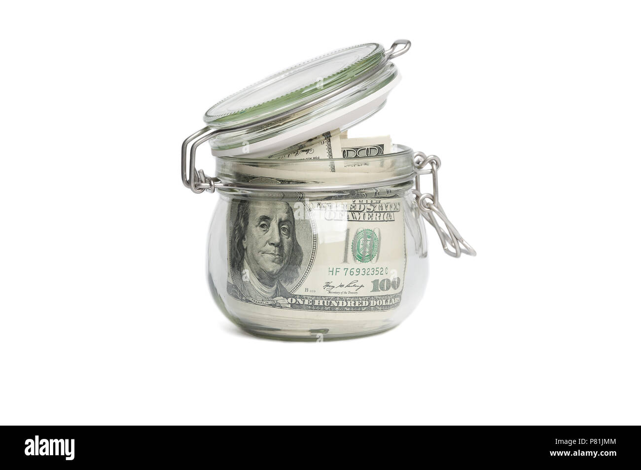 A glass jar filled with dollars among a hundred dollar bills on a white ...