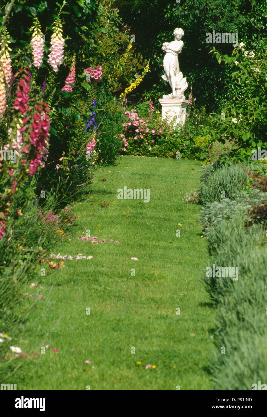 Foxgloves in border beside grass path leading to classical statue in ...