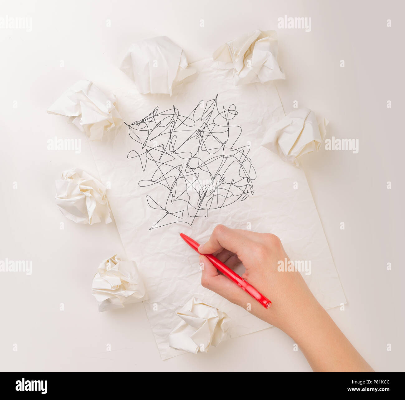 Female hand next to a few crumpled paper balls drawing random scribbles ...