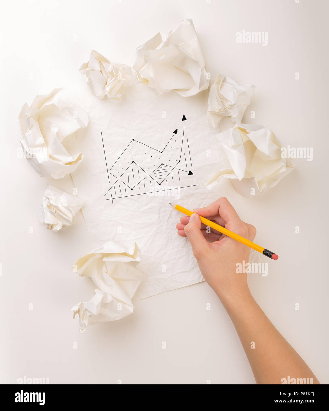 Female hand next to a few crumpled paper balls drawing a progress chart ...