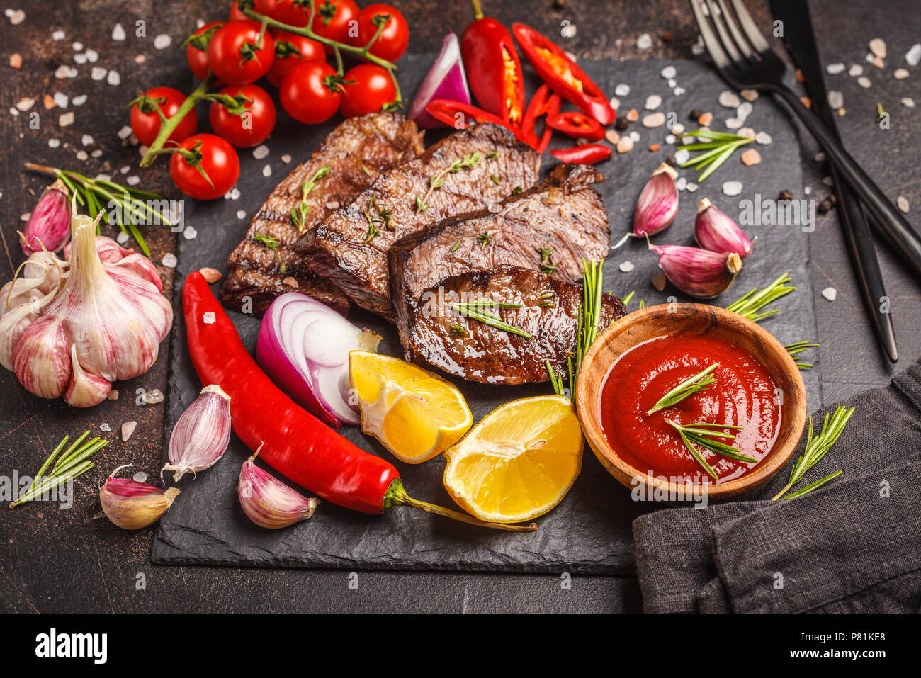 Grilled beef steaks with spices and vegetables on slate board, dark ...