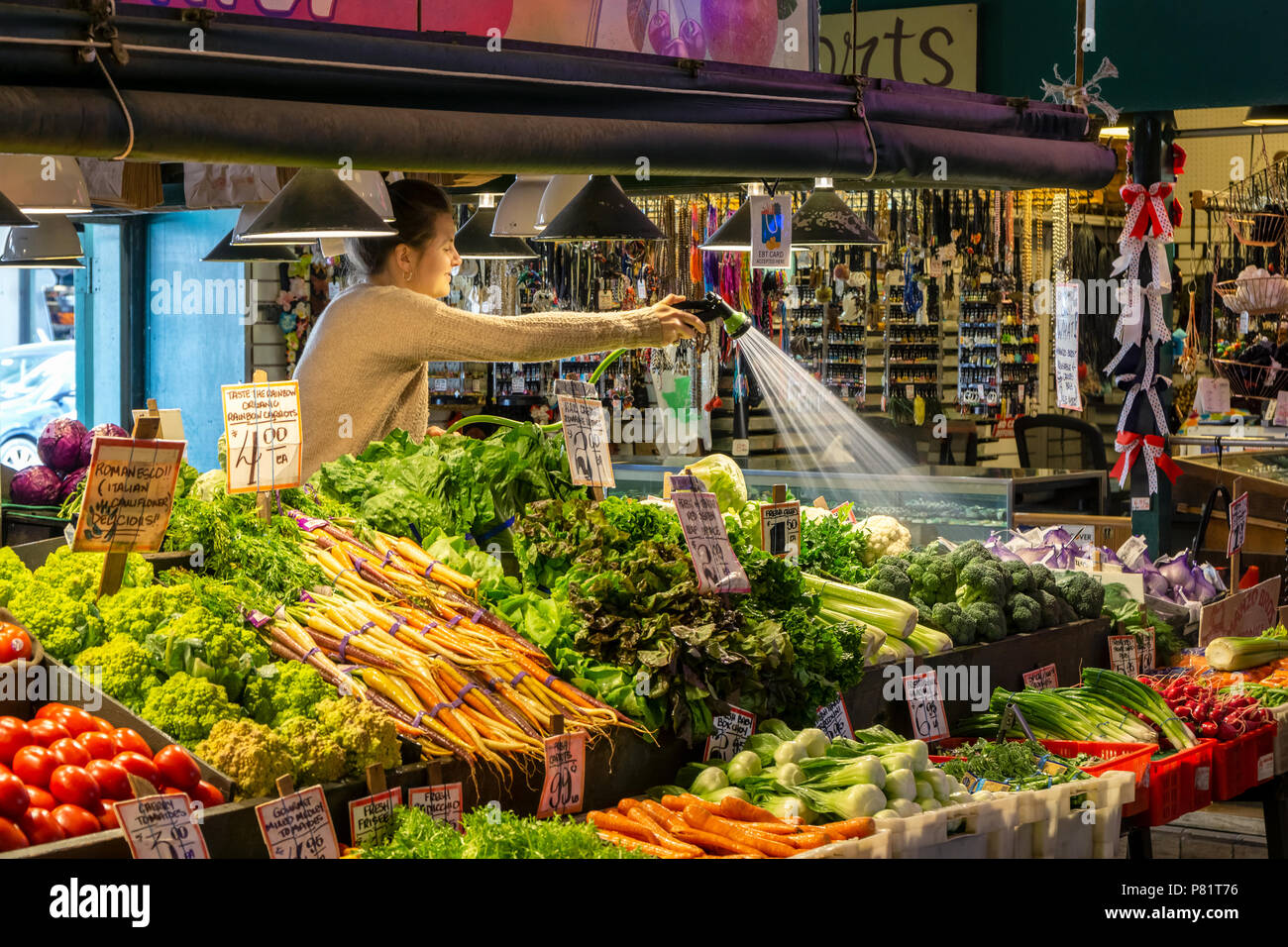 A young vegetable vendor waters her vegetables displayed for sale with ...