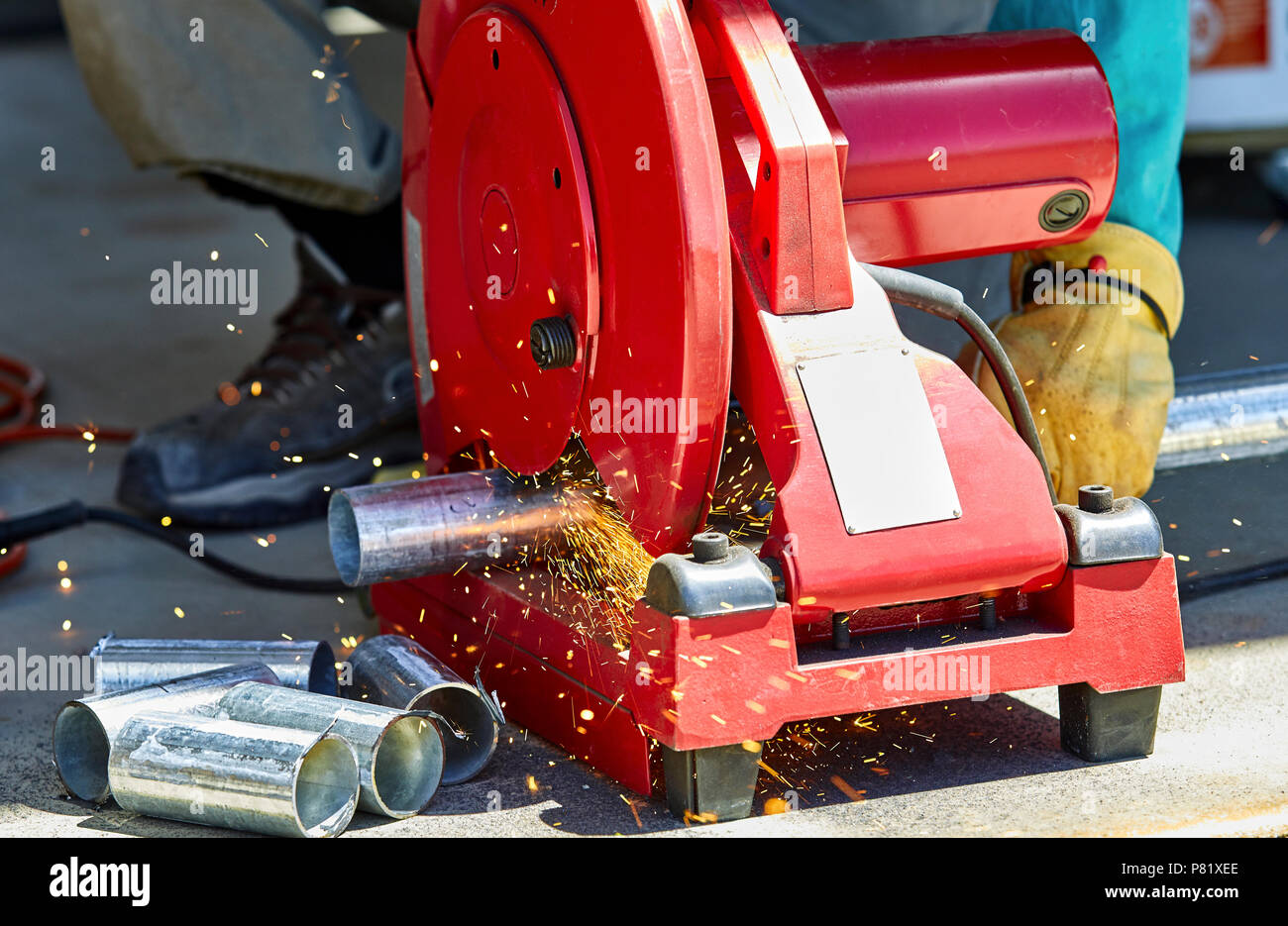 A construction worker cutting a galvanized steel pipe with a chop saw ...