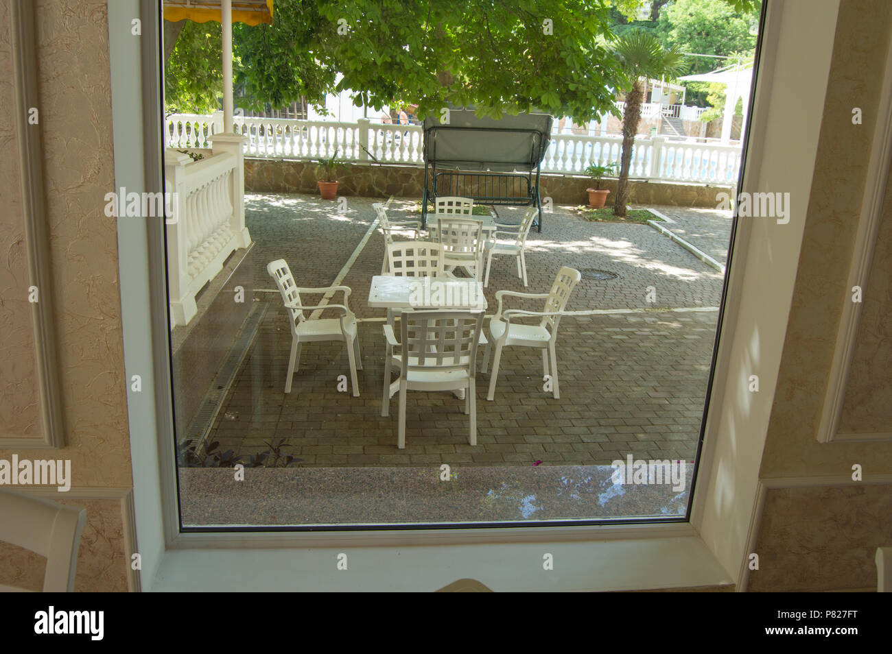 Set of white plastic furniture stands in the patio, view through large ...