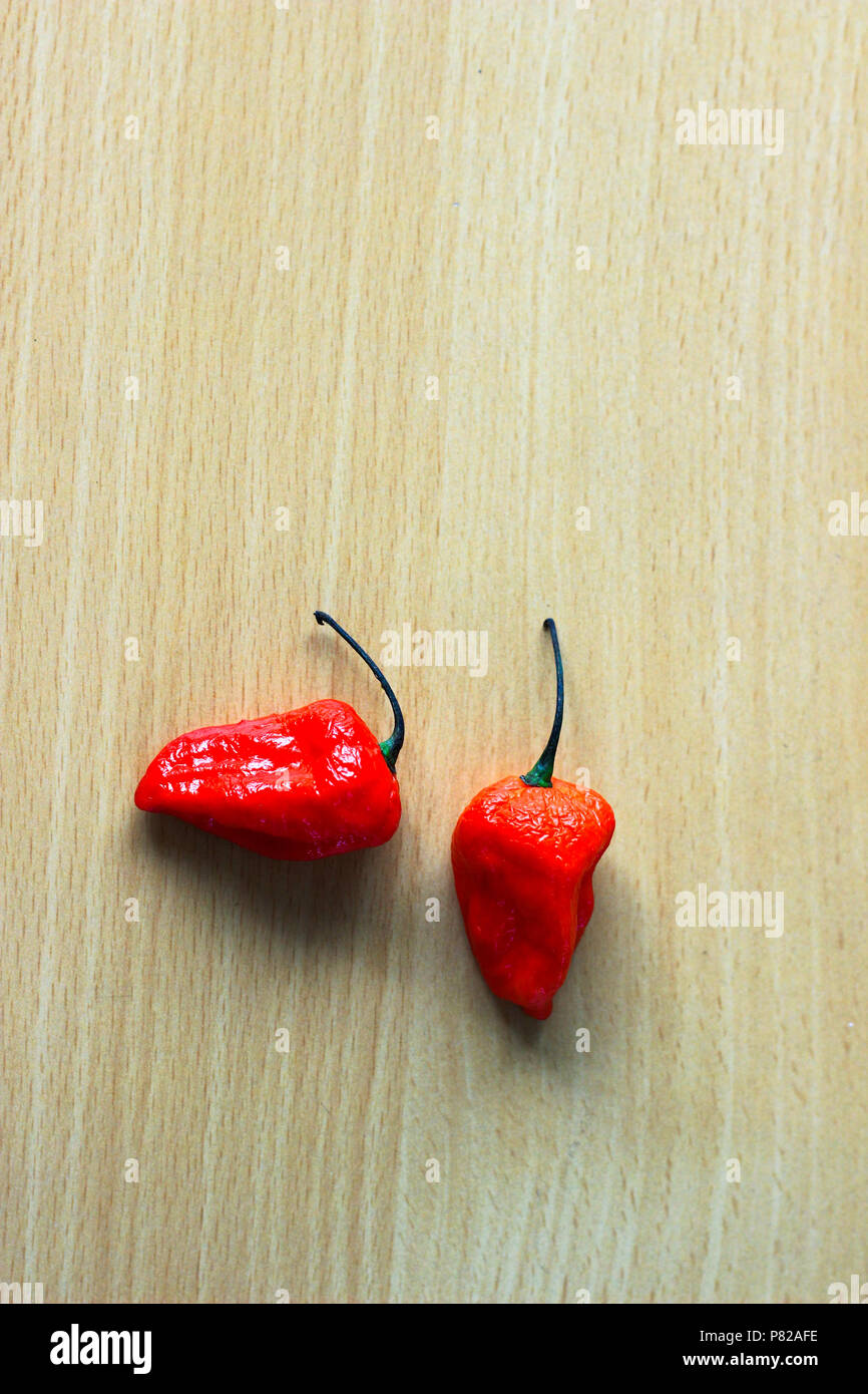 Two Red Bhoot Jolokia Spicy ghost pepper isolated in wooden background ...