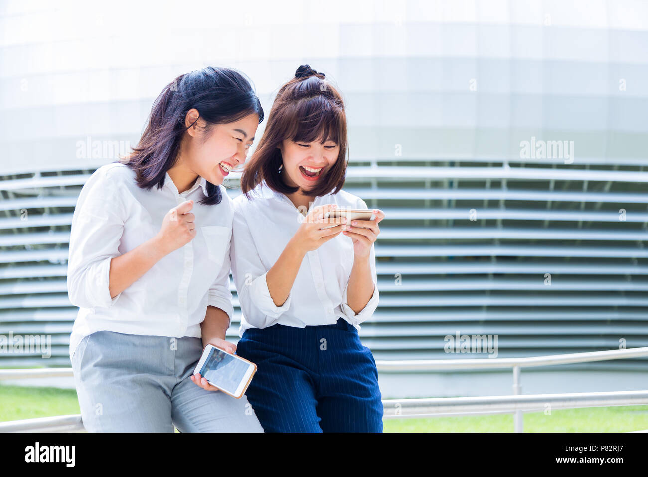Two young Asian women enjoy social media game on their smart phones ...