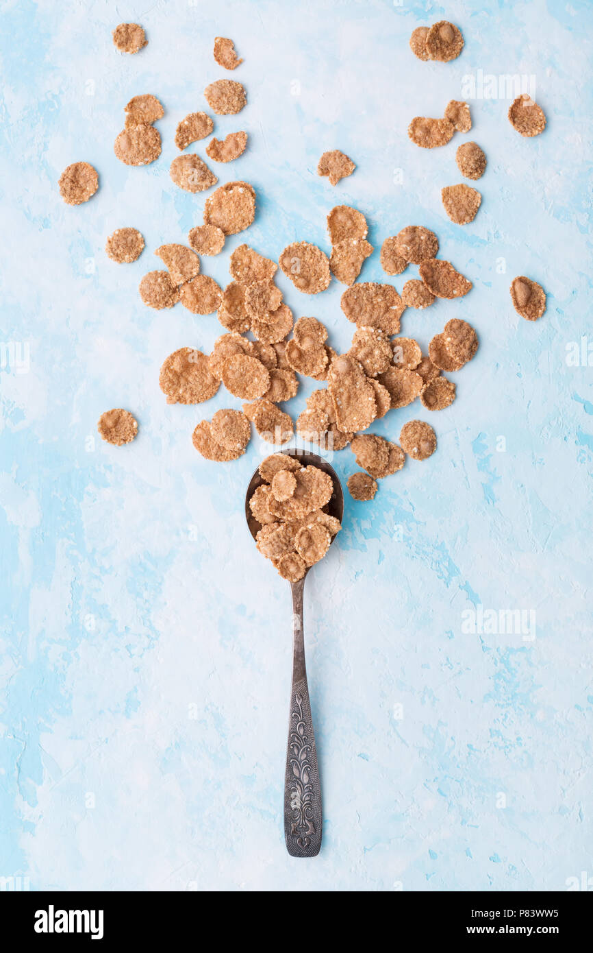 Vintage spoon with scattered corn flakes on blue table. Whole grain ...