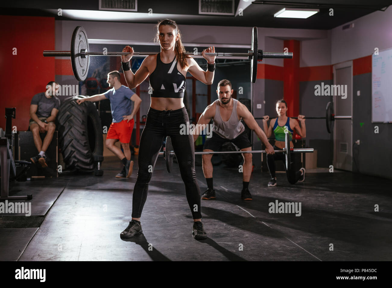 Young muscular woman doing exercise with barbell at the gym. Looking at ...