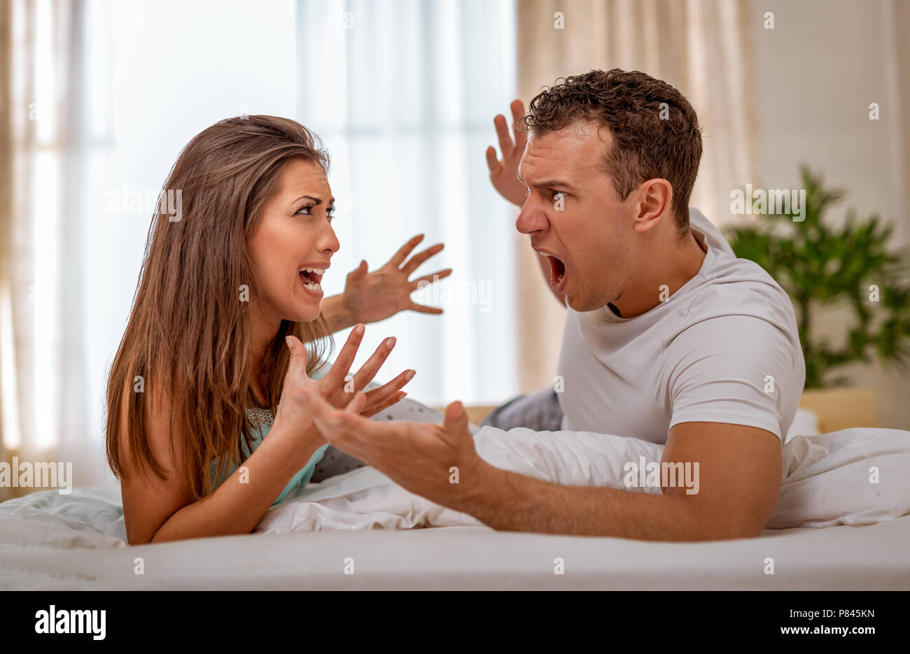 Angry couple is having an argument in bed. They are shouting at each ...