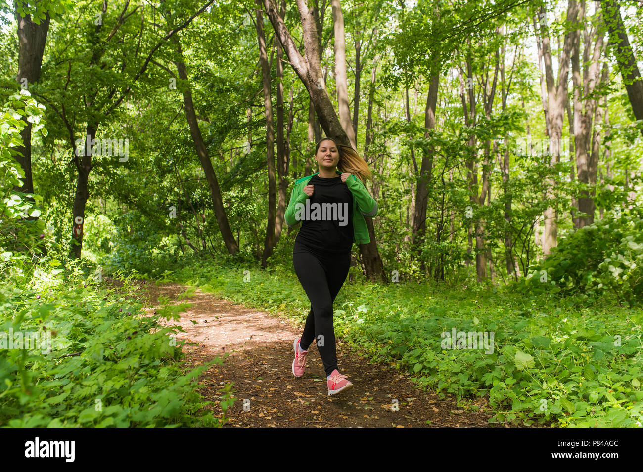 Pretty girl wearing sportswear and running in forest at mountain during ...