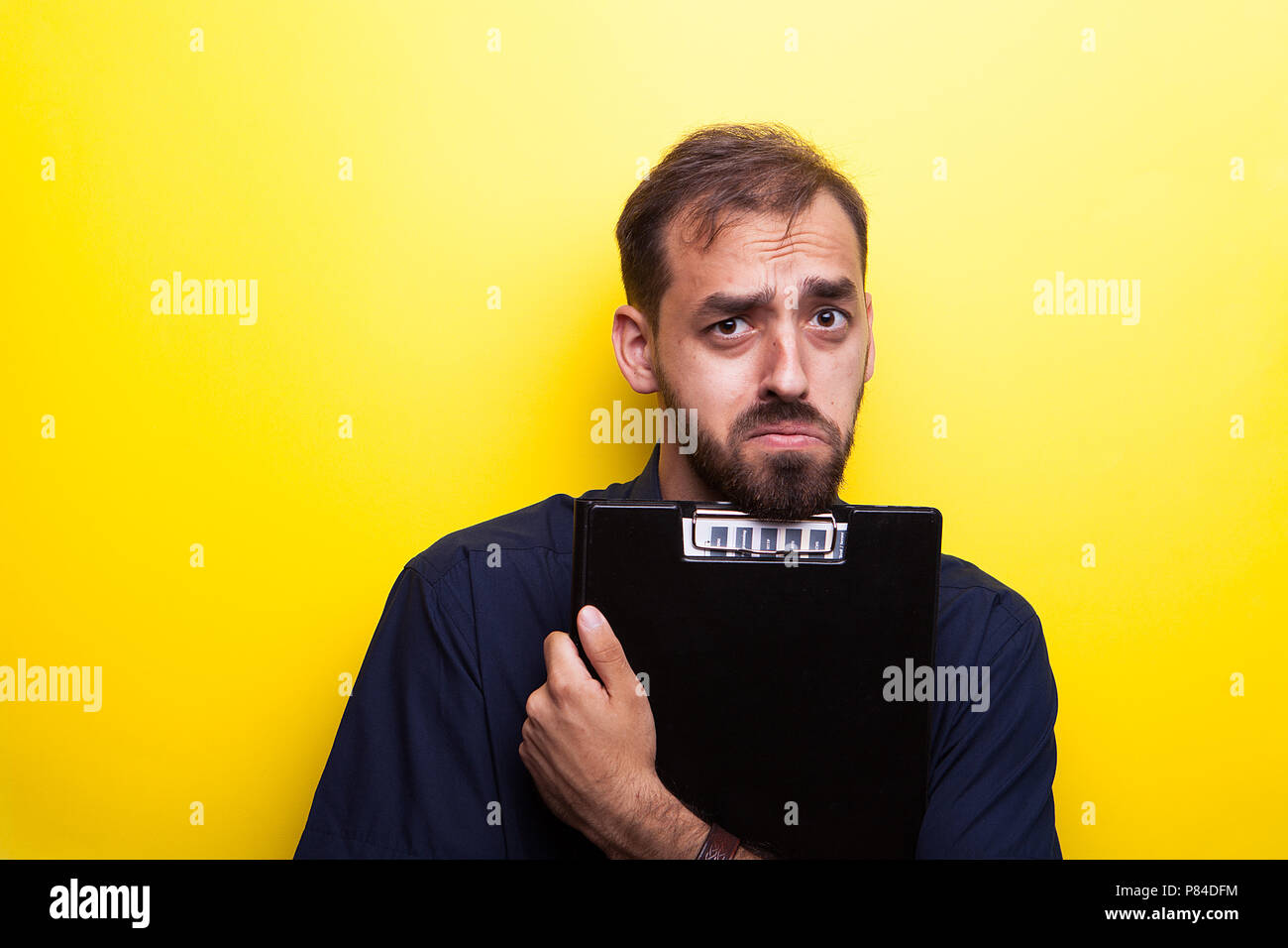 Young man holds a clipboard in hands and makes funny faces. Yellow ...