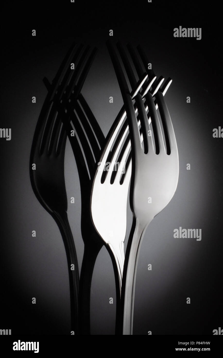 Two interlocking shiny forks on reflective black background for ...