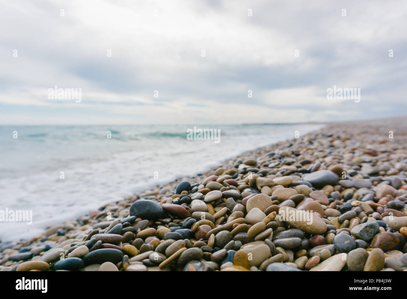 Wet pebbles lying on beach near waving sea on cloudy day Stock Photo ...