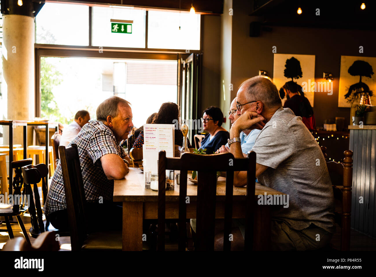 Two men sit opposite each other across a table in a cafe bar talking ...