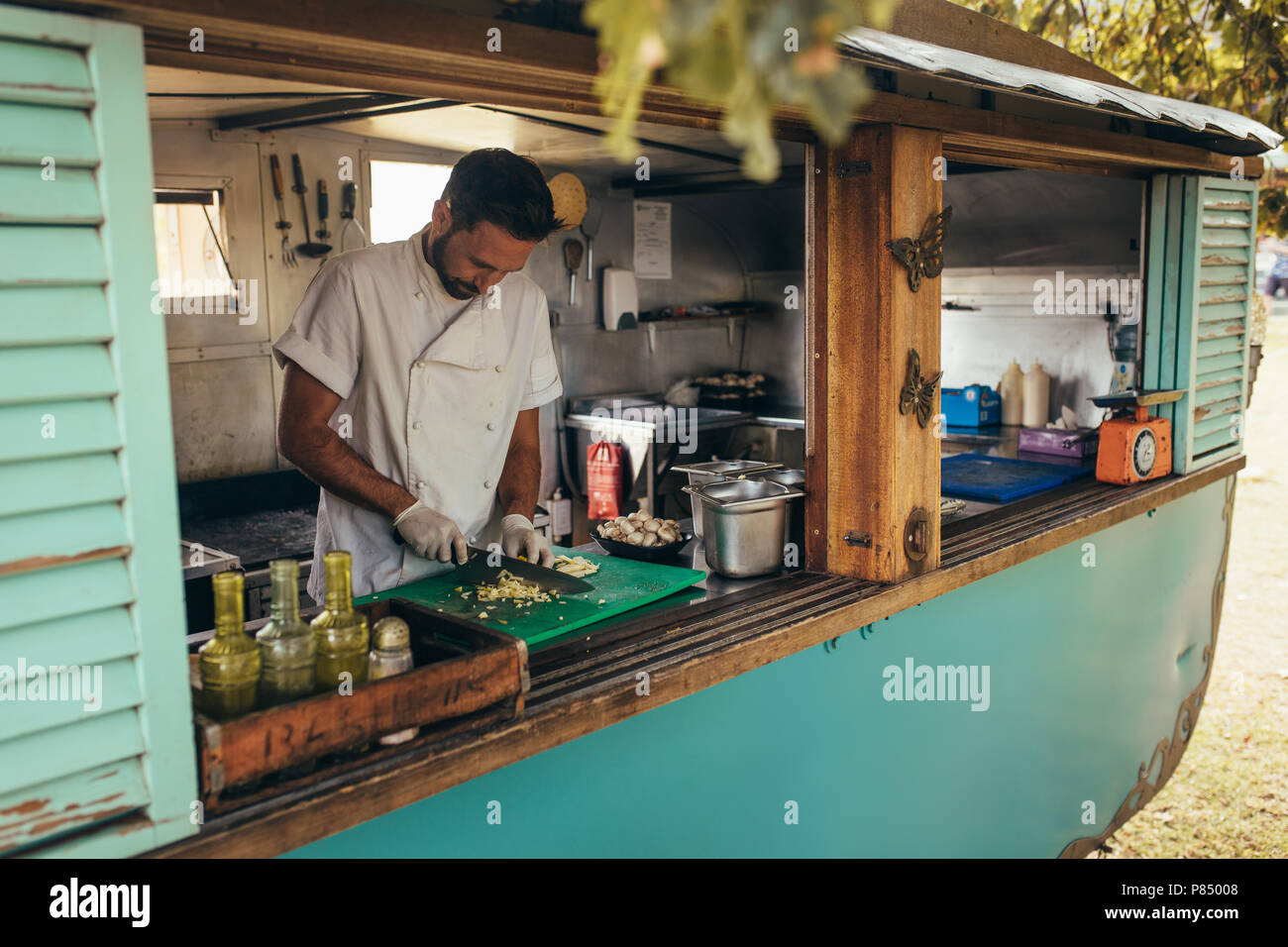 Man cooking some food in a mobile food truck parked under a tree. Man ...