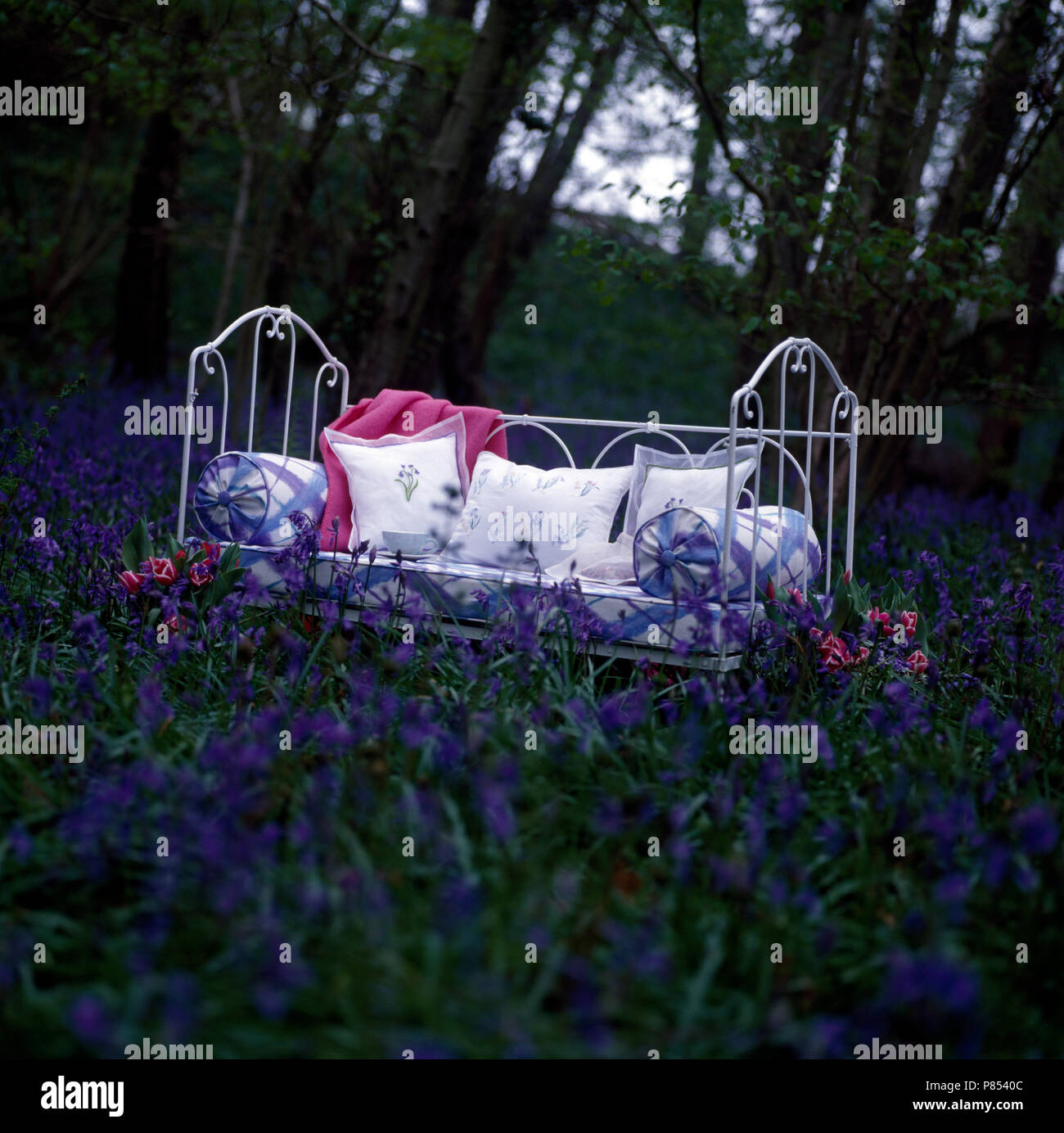 A metal day bed piled with cushions in a bluebell wood Stock Photo - Alamy