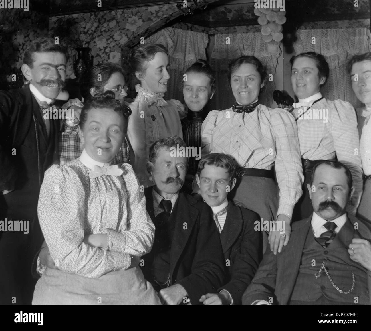 A group of turn of the century adults smile and gather for a group ...