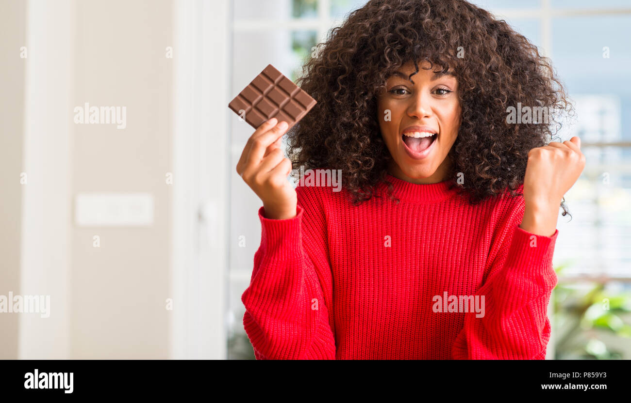 African american woman eating chocolate bar at home screaming proud and ...