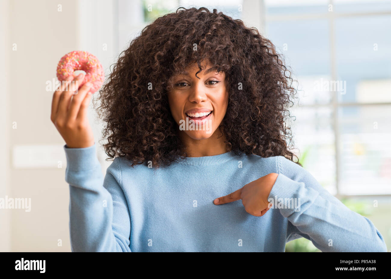 African american woman holding donut at home with surprise face ...