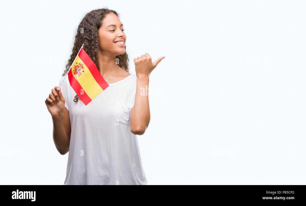 Young hispanic woman holding flag of Spain pointing and showing with ...