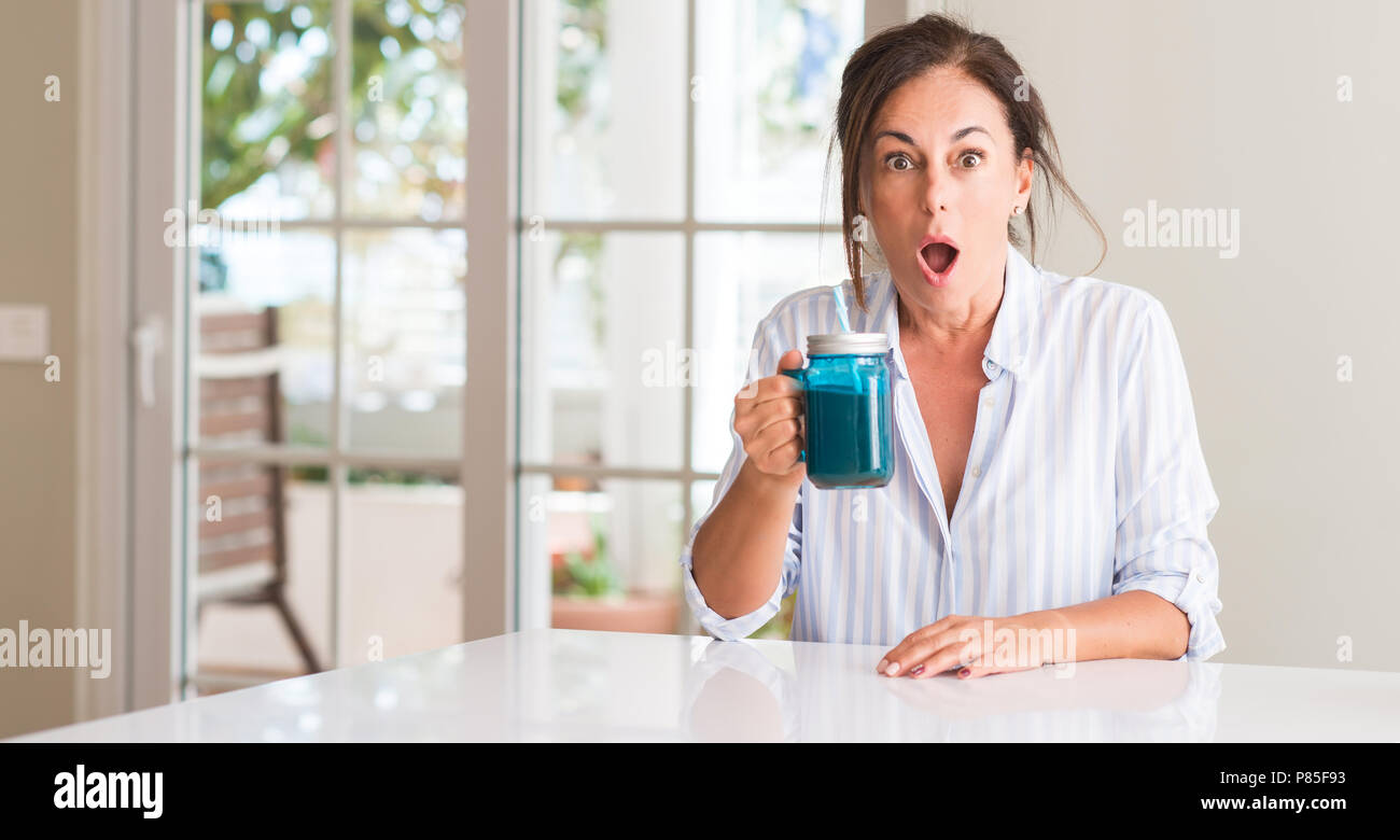 Middle aged woman drinking milk shake in a glass scared in shock with a ...