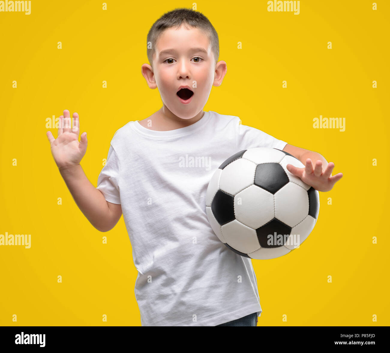 Dark haired little child playing with soccer ball scared in shock with ...