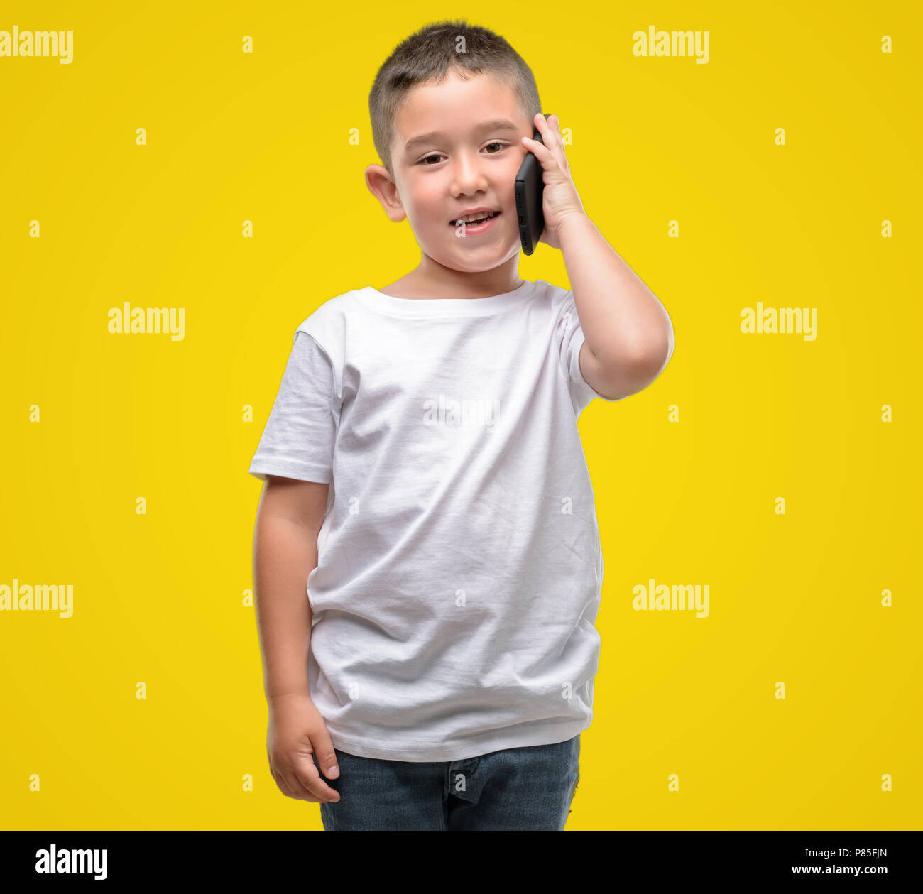 Dark haired little child using a smartphone with a happy face standing ...