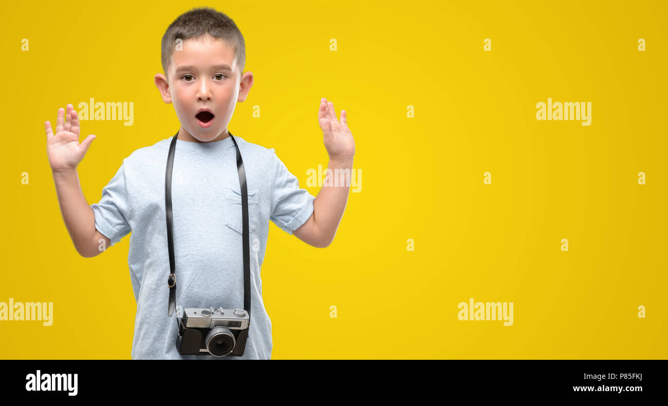 Dark haired little child holding vintage camera scared in shock with a ...