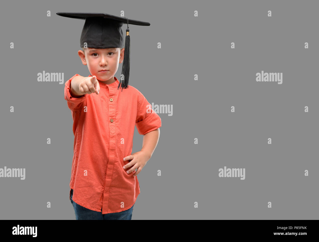 Dark haired little child wearing graduation cap pointing with finger to ...