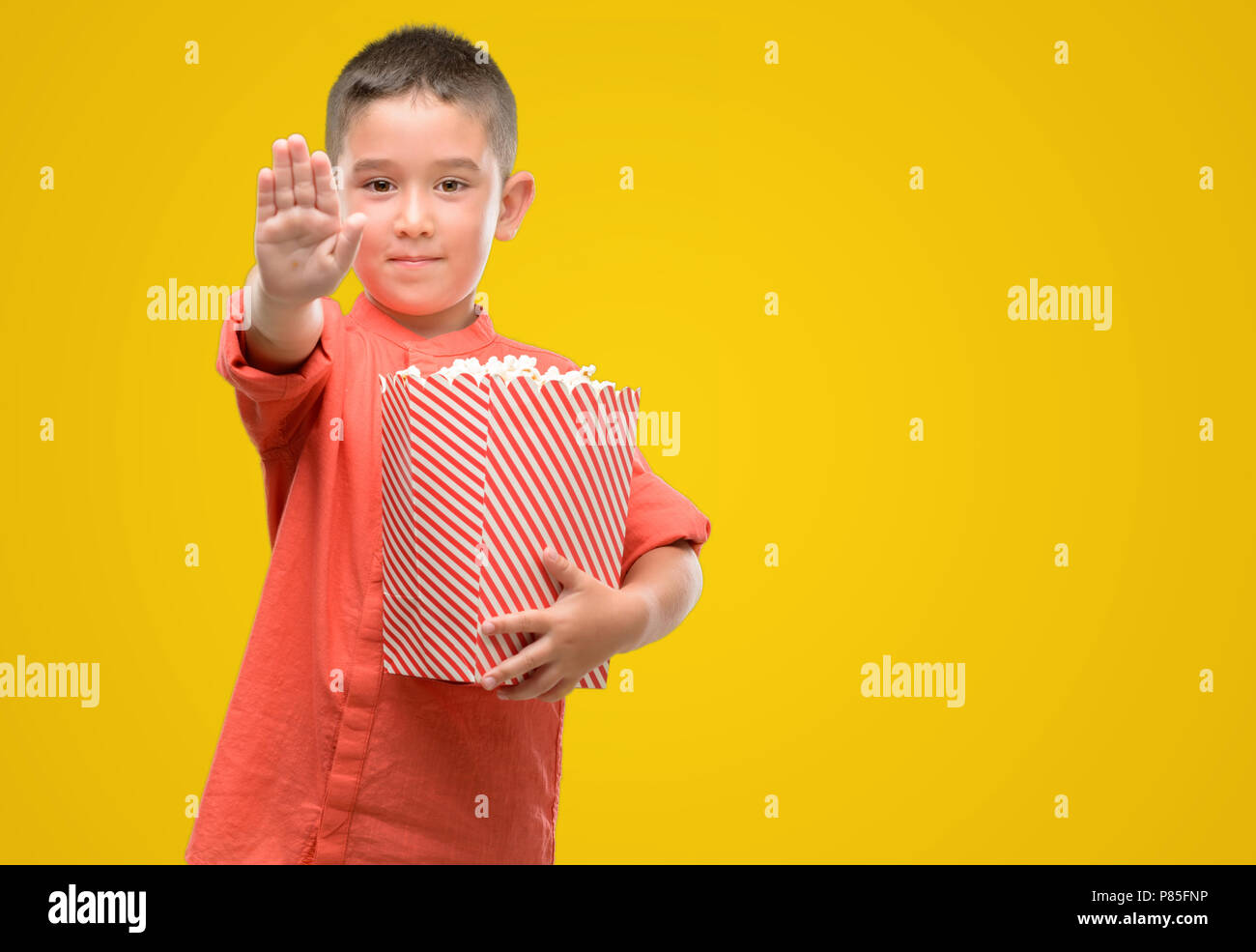 Dark haired little child eating popcorn with open hand doing stop sign ...