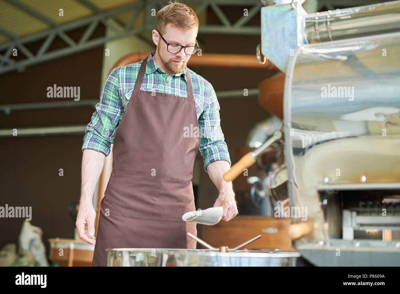 Portrait of modern young man wearing apron and glasses taking scoop of ...