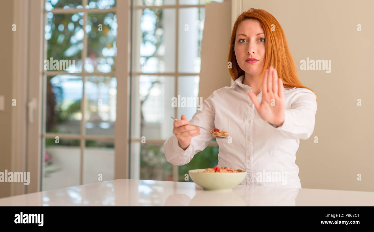 Redhead woman eating cereals with raspberries at home with open hand ...