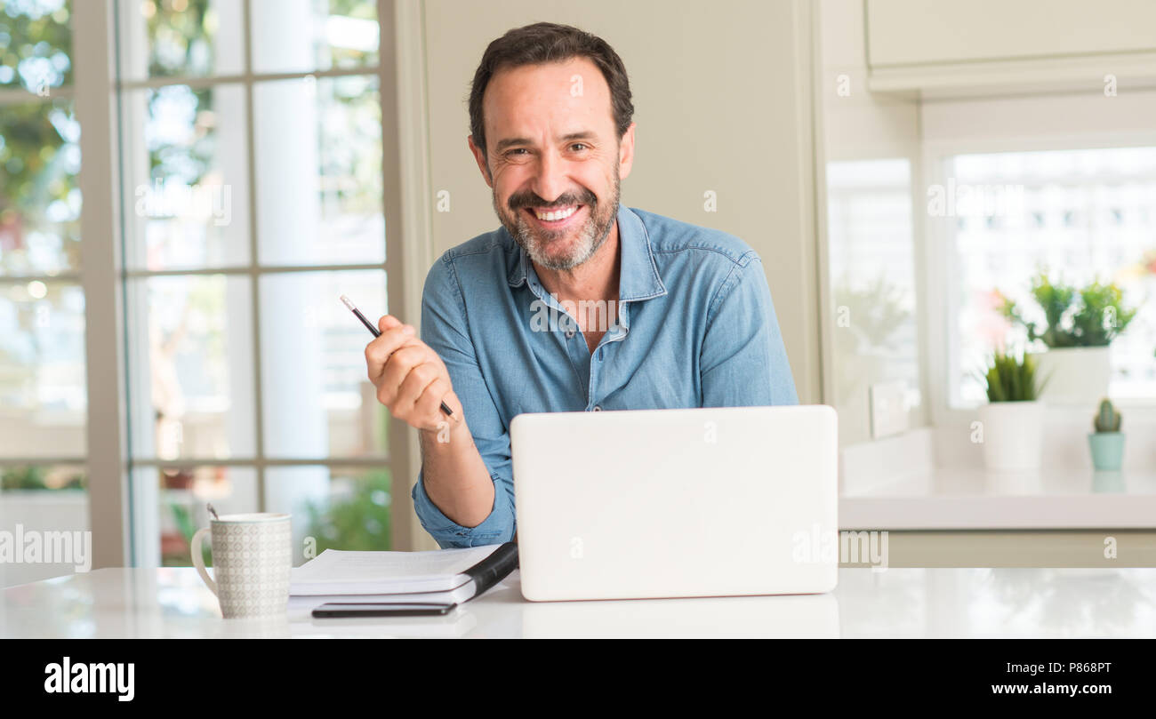 Middle age man using laptop at home with a happy face standing and ...