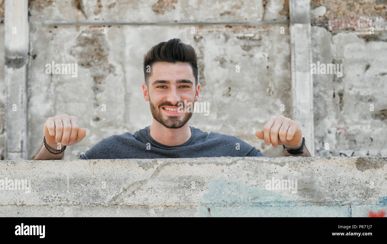 Young man popping out from behind a small wall in an abandoned building ...