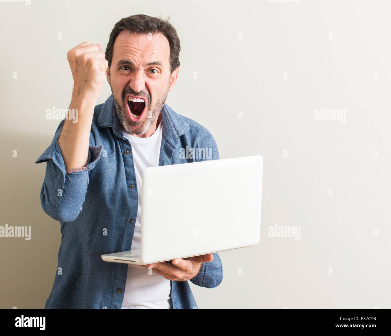 Senior man using laptop computer annoyed and frustrated shouting with ...