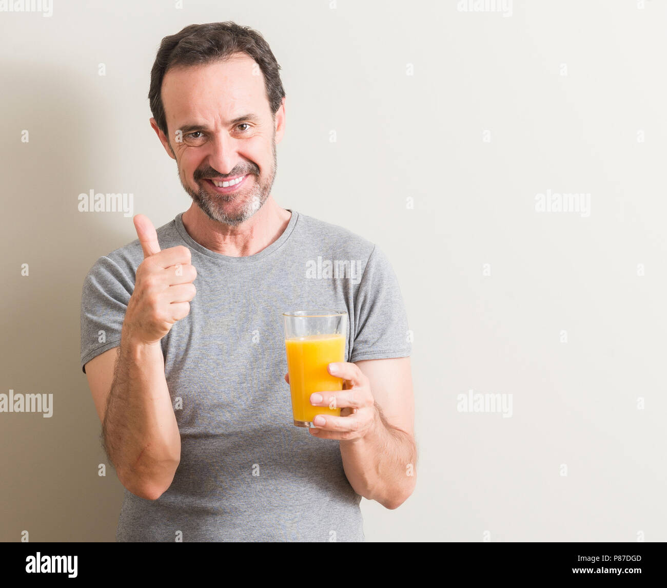 Senior man drinking orange juice in a glass happy with big smile doing ...
