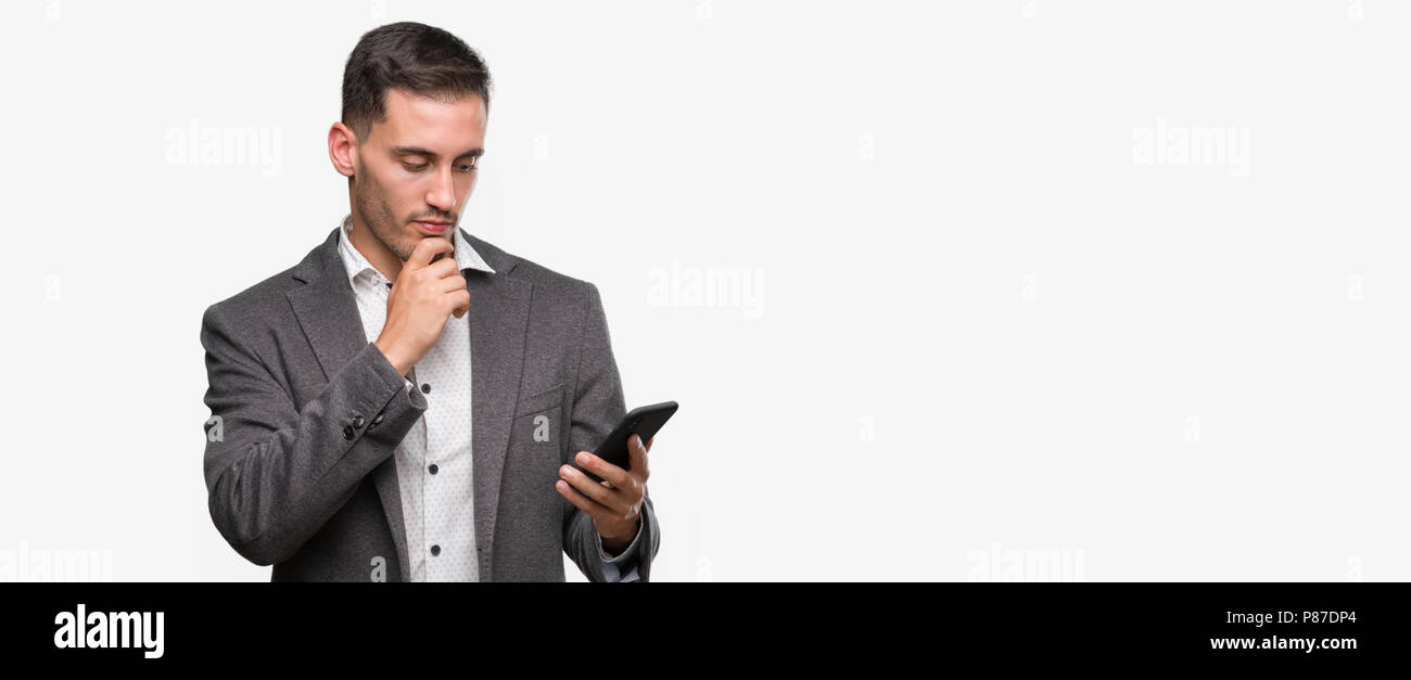 Handsome young man using smartphone serious face thinking about ...
