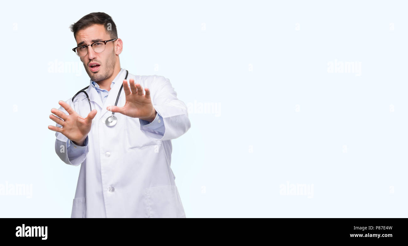 Handsome young doctor man afraid and terrified with fear expression ...