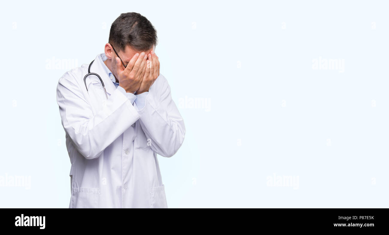 Handsome young doctor man with sad expression covering face with hands ...