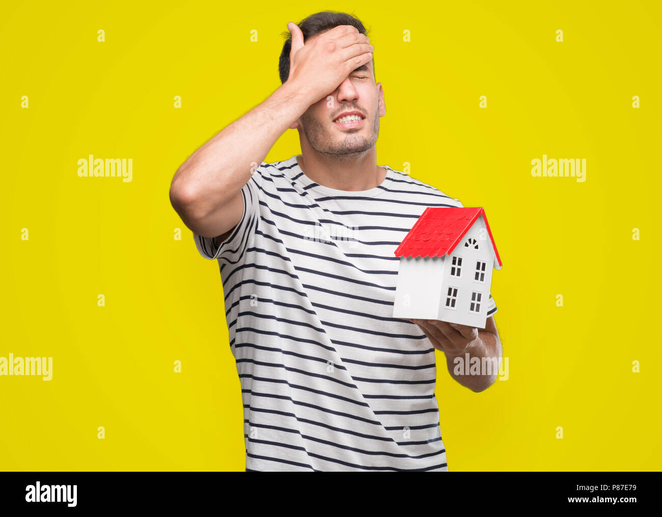Handsome real estate agent holding a house stressed with hand on head ...
