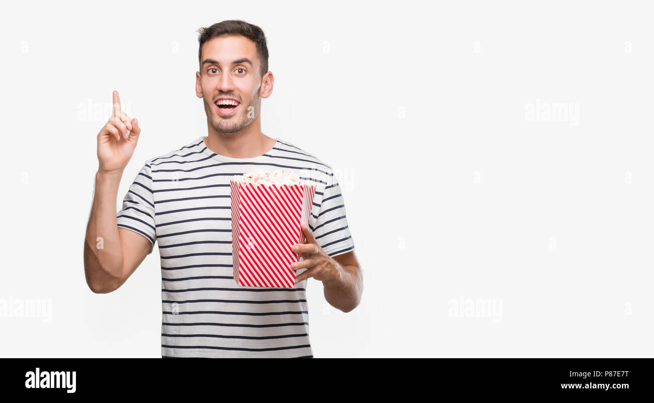 Handsome young man eating popcorn surprised with an idea or question ...
