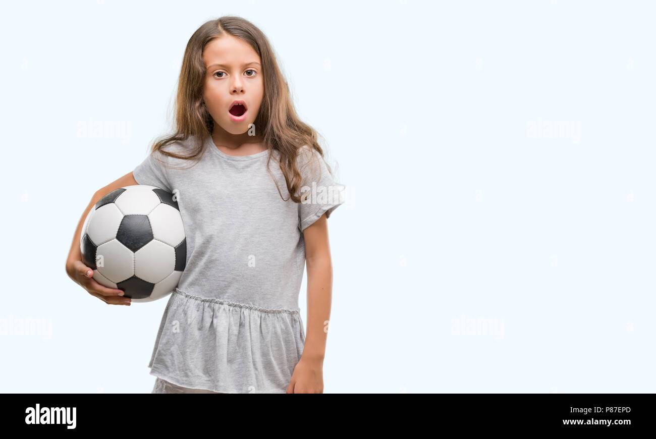 Brunette hispanic girl holding soccer football ball scared in shock ...