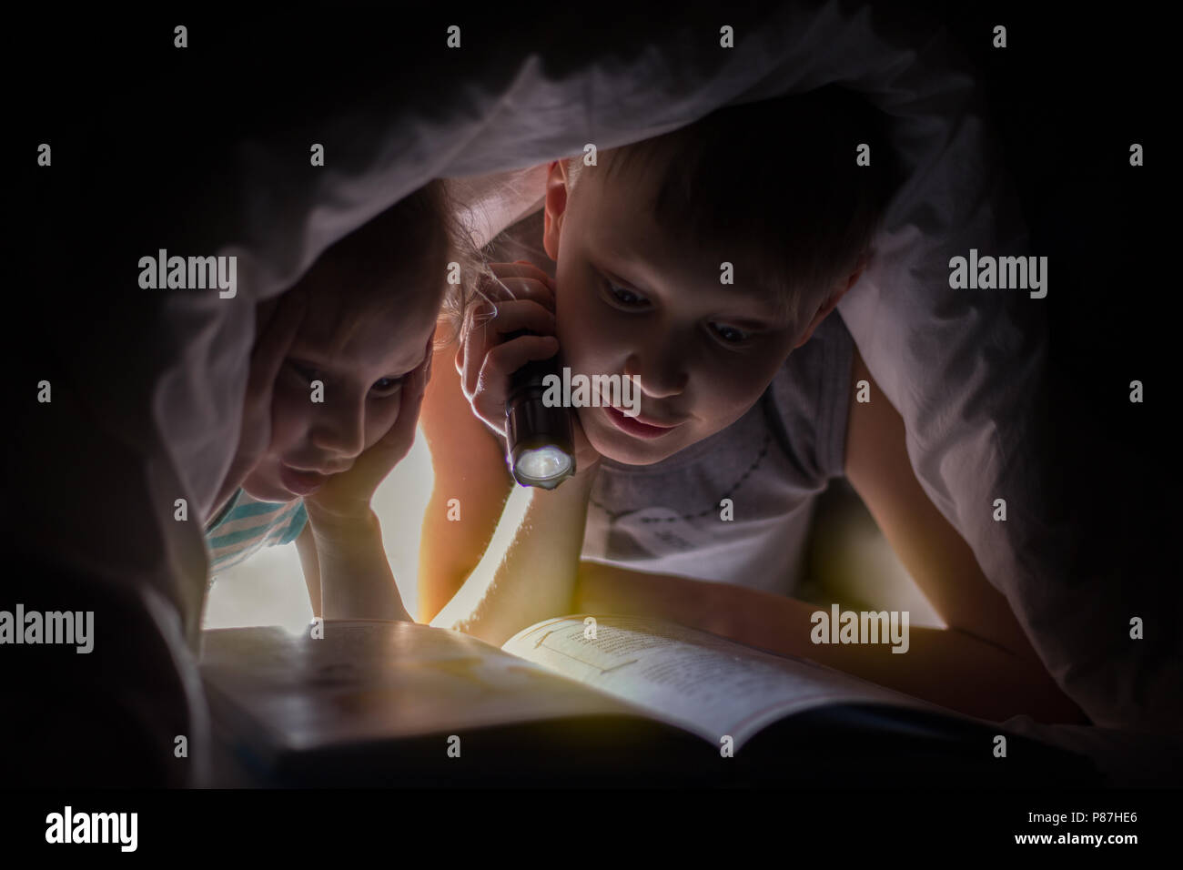 Children bedtime. Sister and brother are reading a book under a blanket ...