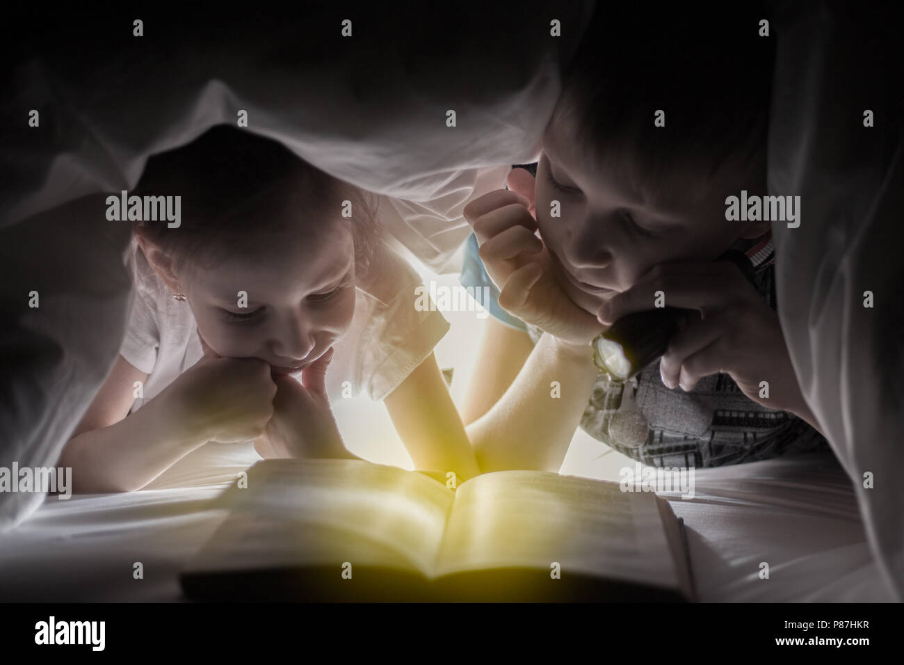 Children bedtime. Sister and brother are reading a book under a blanket ...