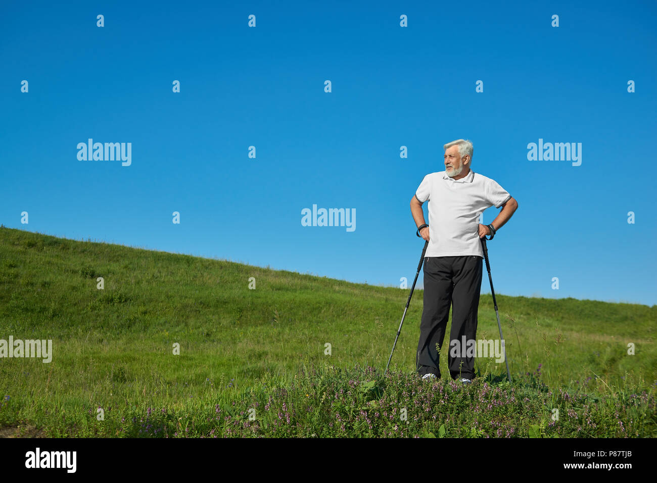 Man wearing sportsuit standing with tracking sticks on green hill ...