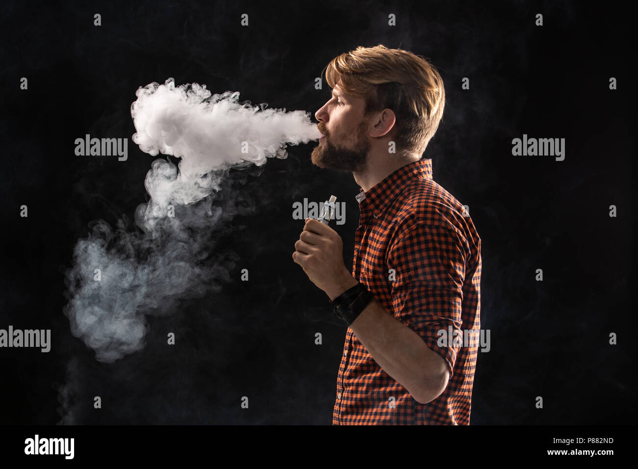 A young man with a beard and a stylish hairstyle in a shirt, smoking a ...