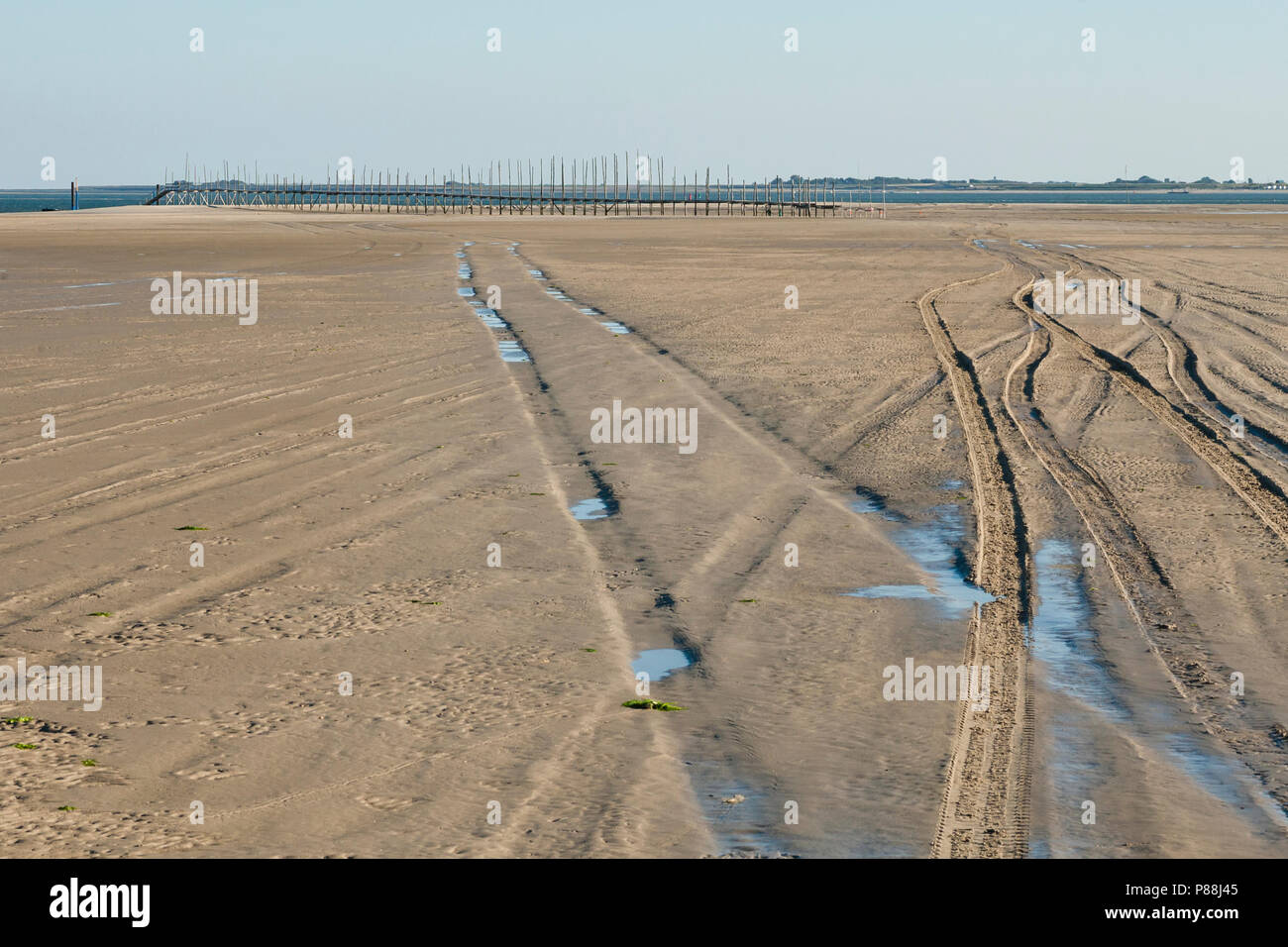 Weids uitzicht over het strand met bandensporen en aanlegsteiger ...